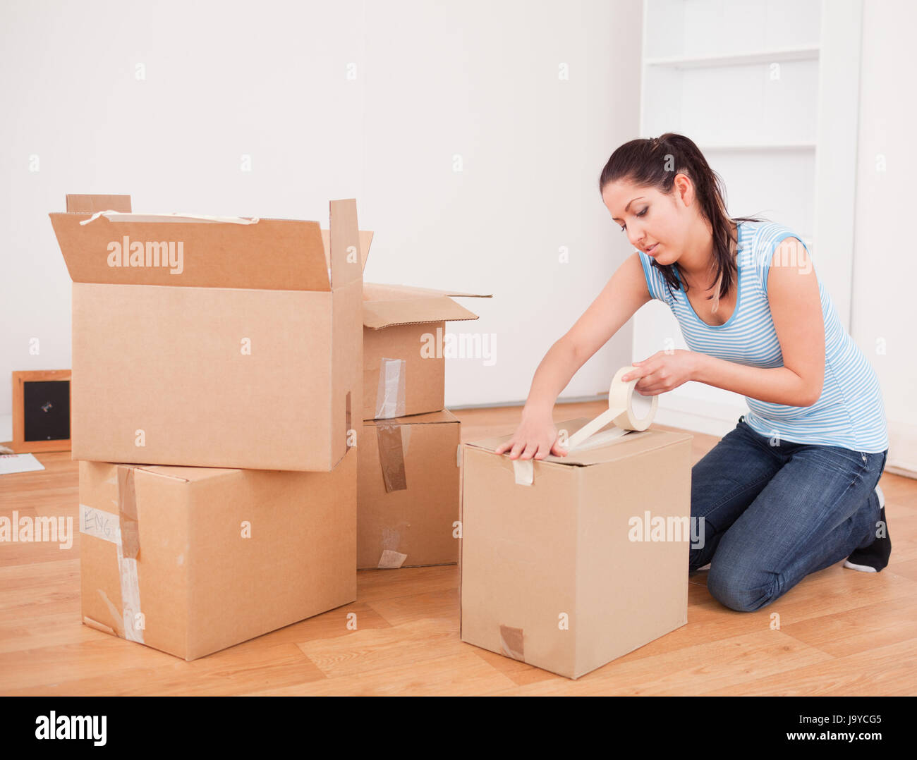 Pretty woman taping a box kneeling a hand on the box Stock Photo - Alamy