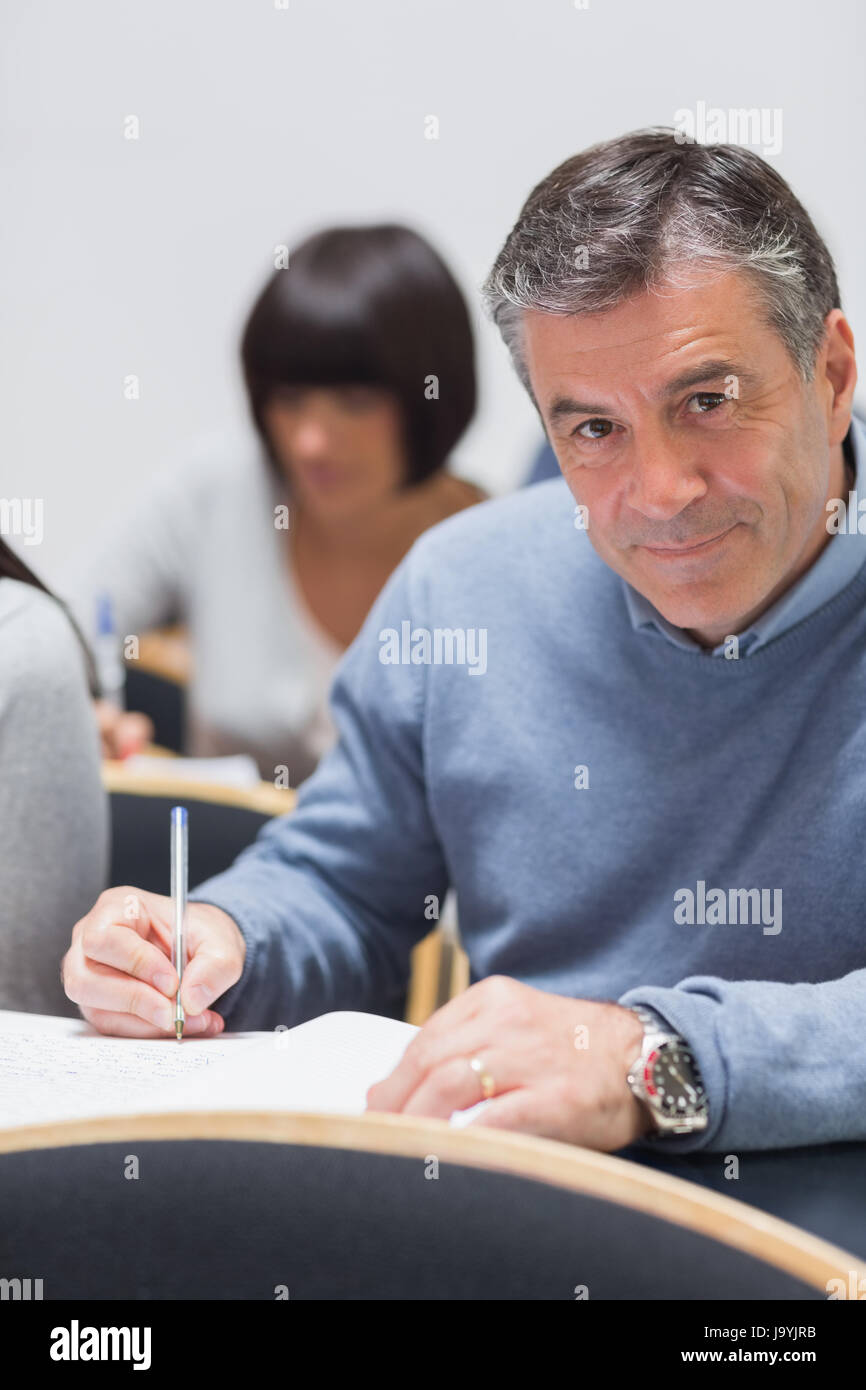 Man looking up from taking notes and smiling in a lecture in college ...