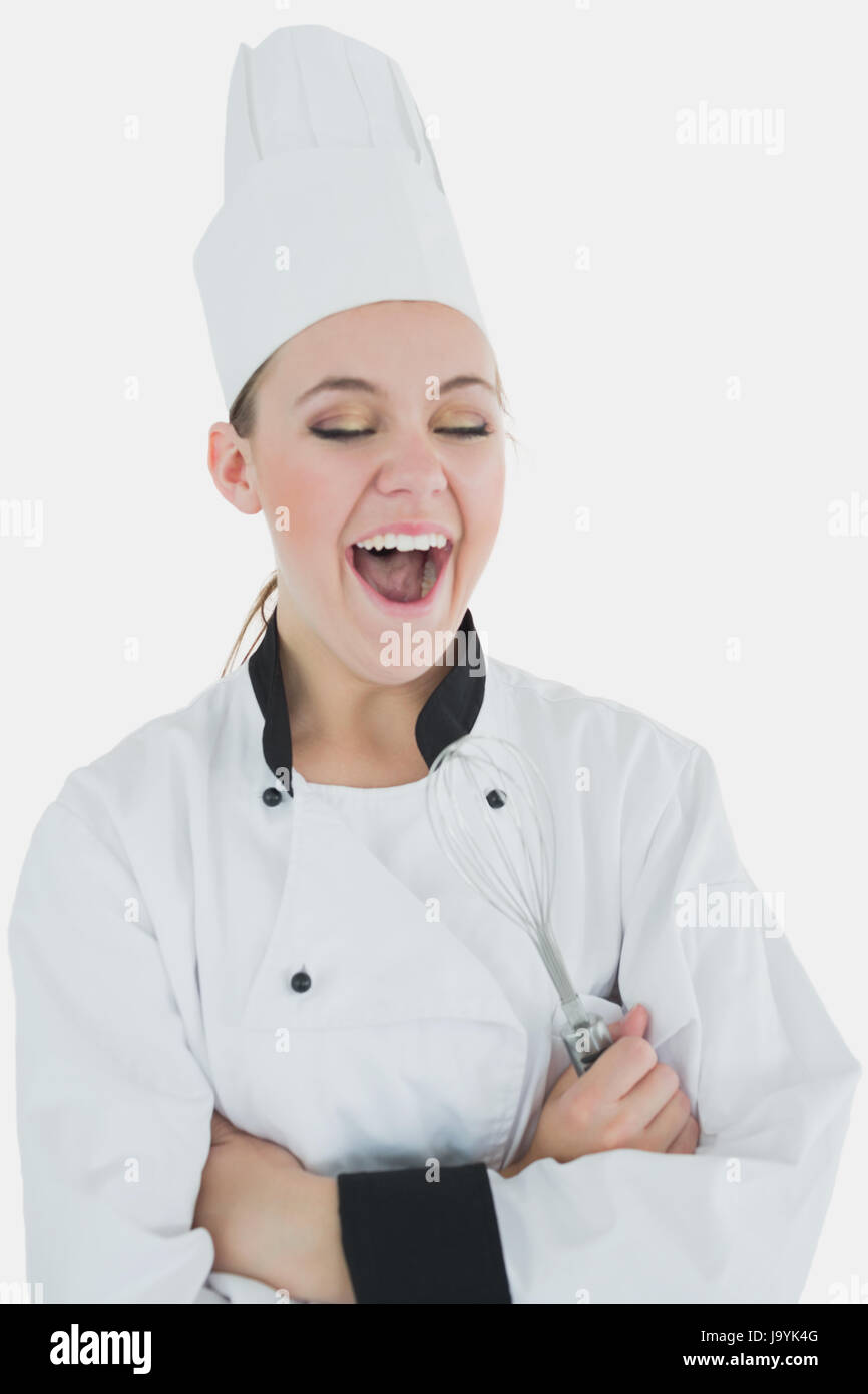 Female chef holding wire whisk as she laughs over white background ...