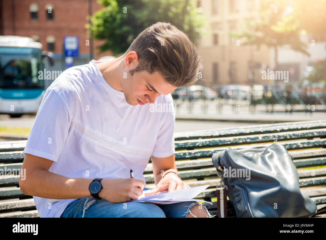 Young man sitting on bench writing on notepad hi-res stock photography ...