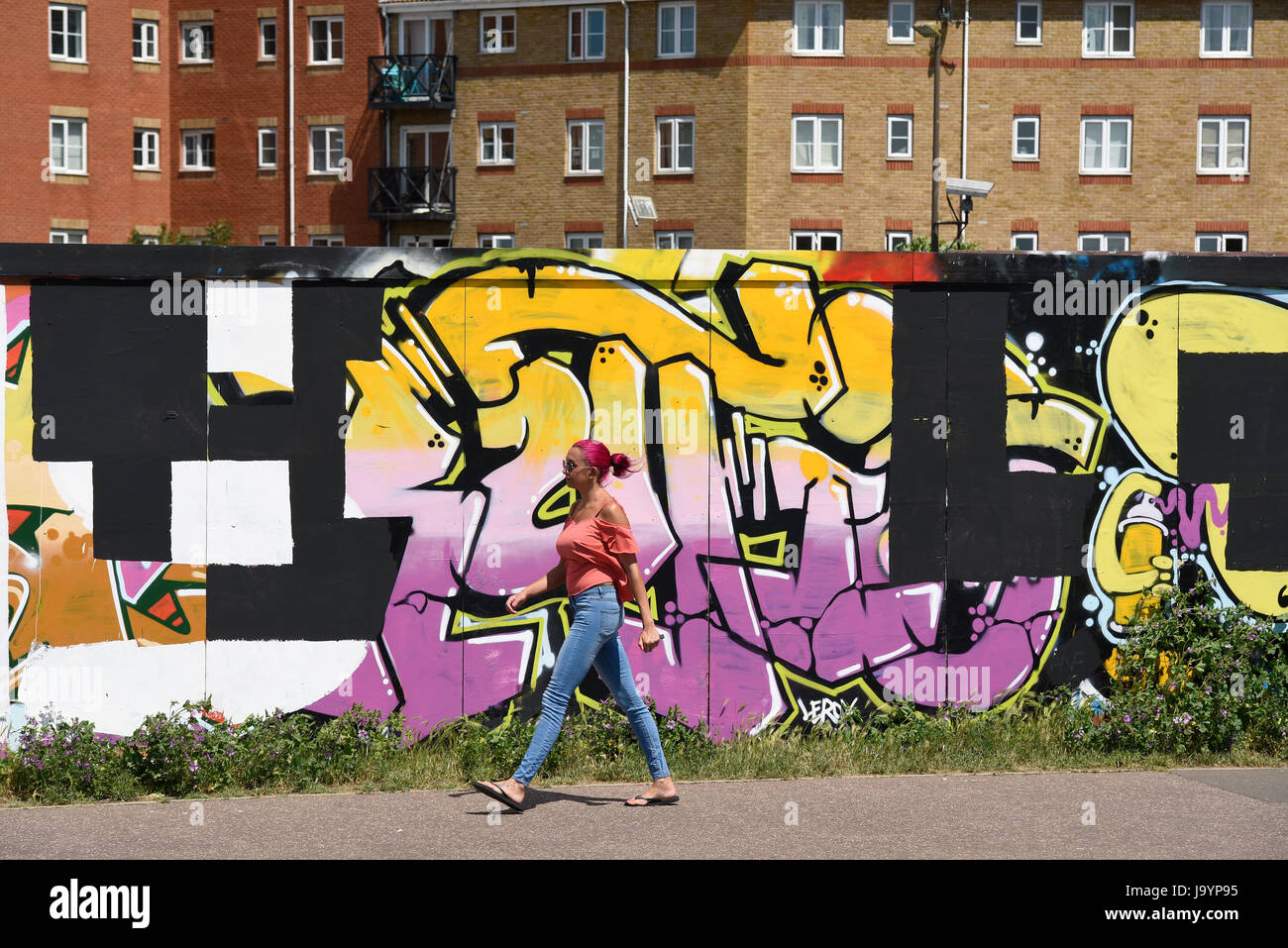 A female walking past graffiti on a building site hoarding. Graffiti ...