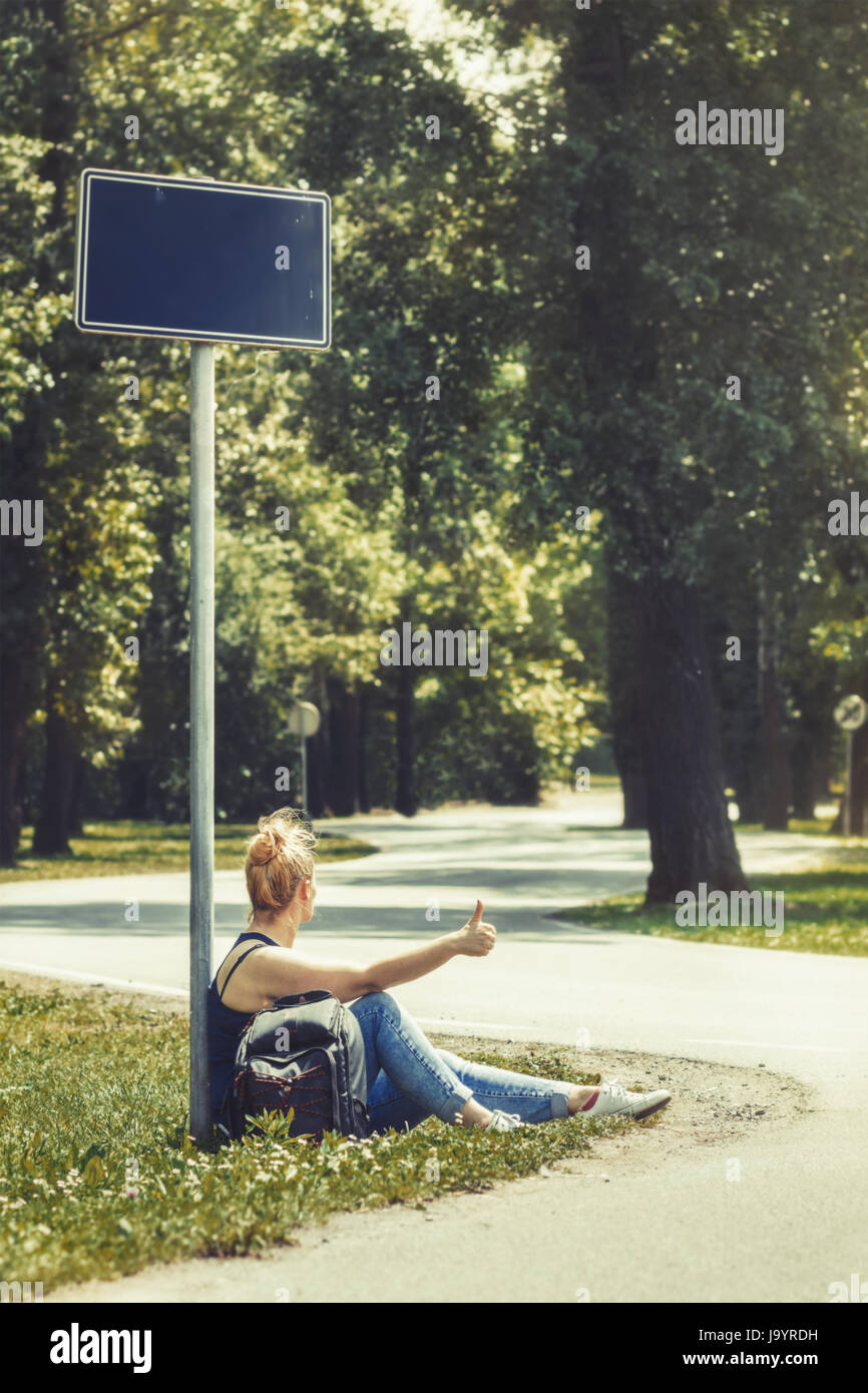 Woman sitting on a side of the road under the street sign, surrounded ...