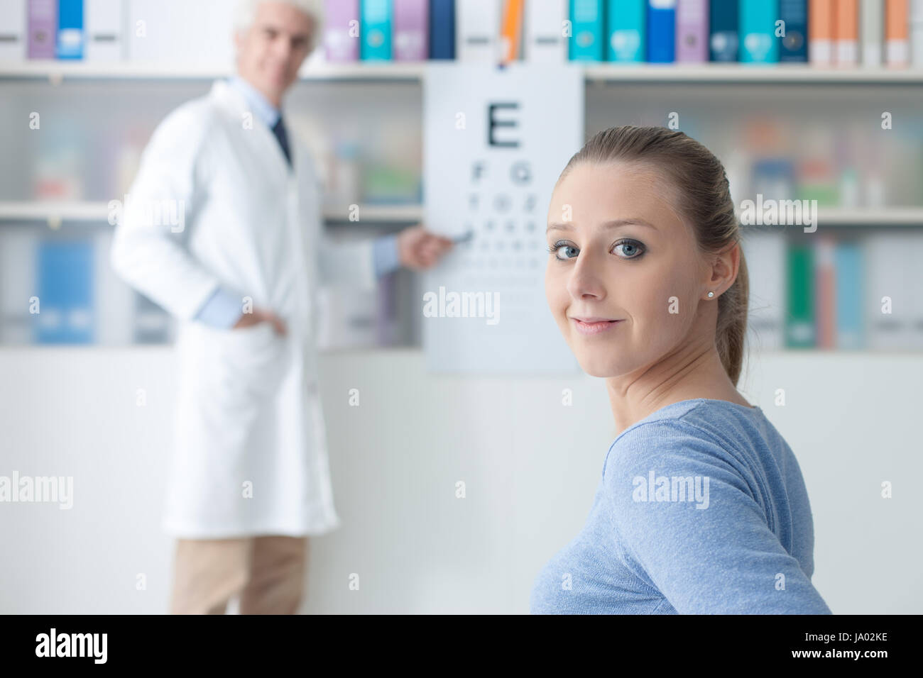 Young woman in the optometrist office examining her eyesight, he is pointing at the chart, eye ...