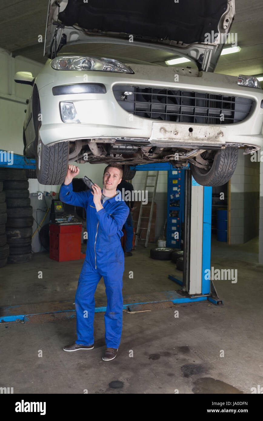 Full length portrait of male mechanic working under raised car in ...
