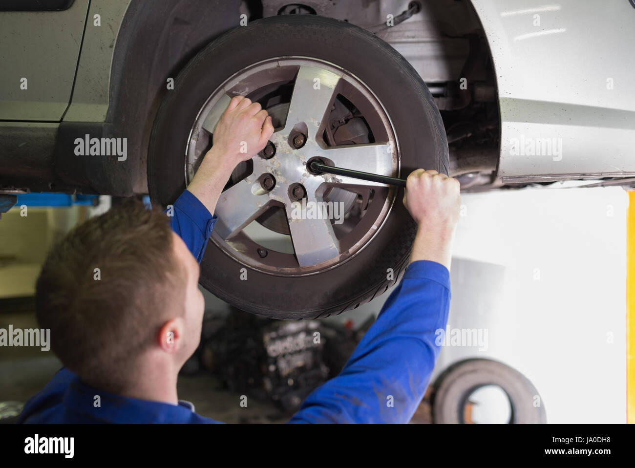 Rear view of male mechanic fixing car tire Stock Photo - Alamy
