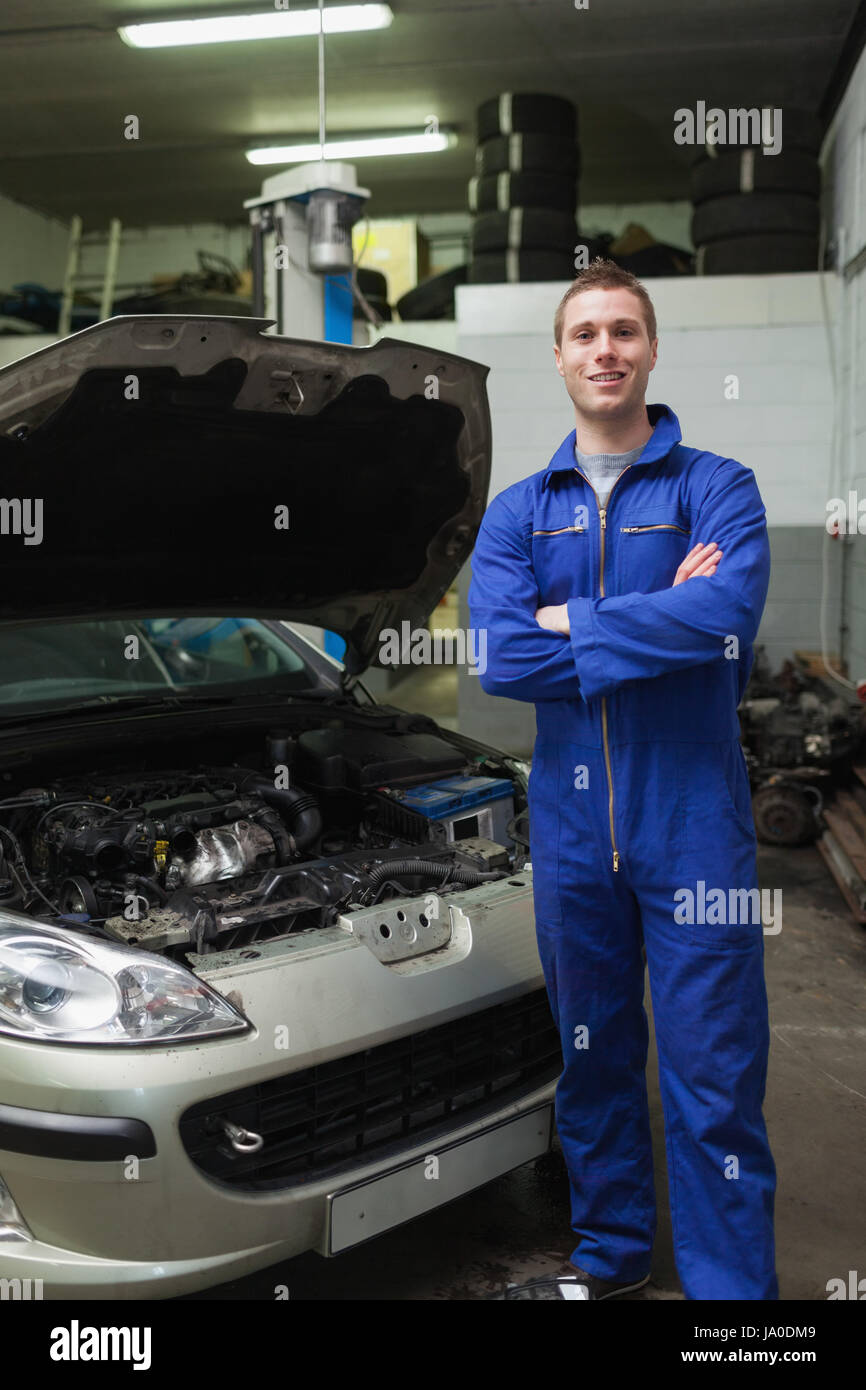 Portrait of young male mechanic with arms crossed standing by breakdown ...