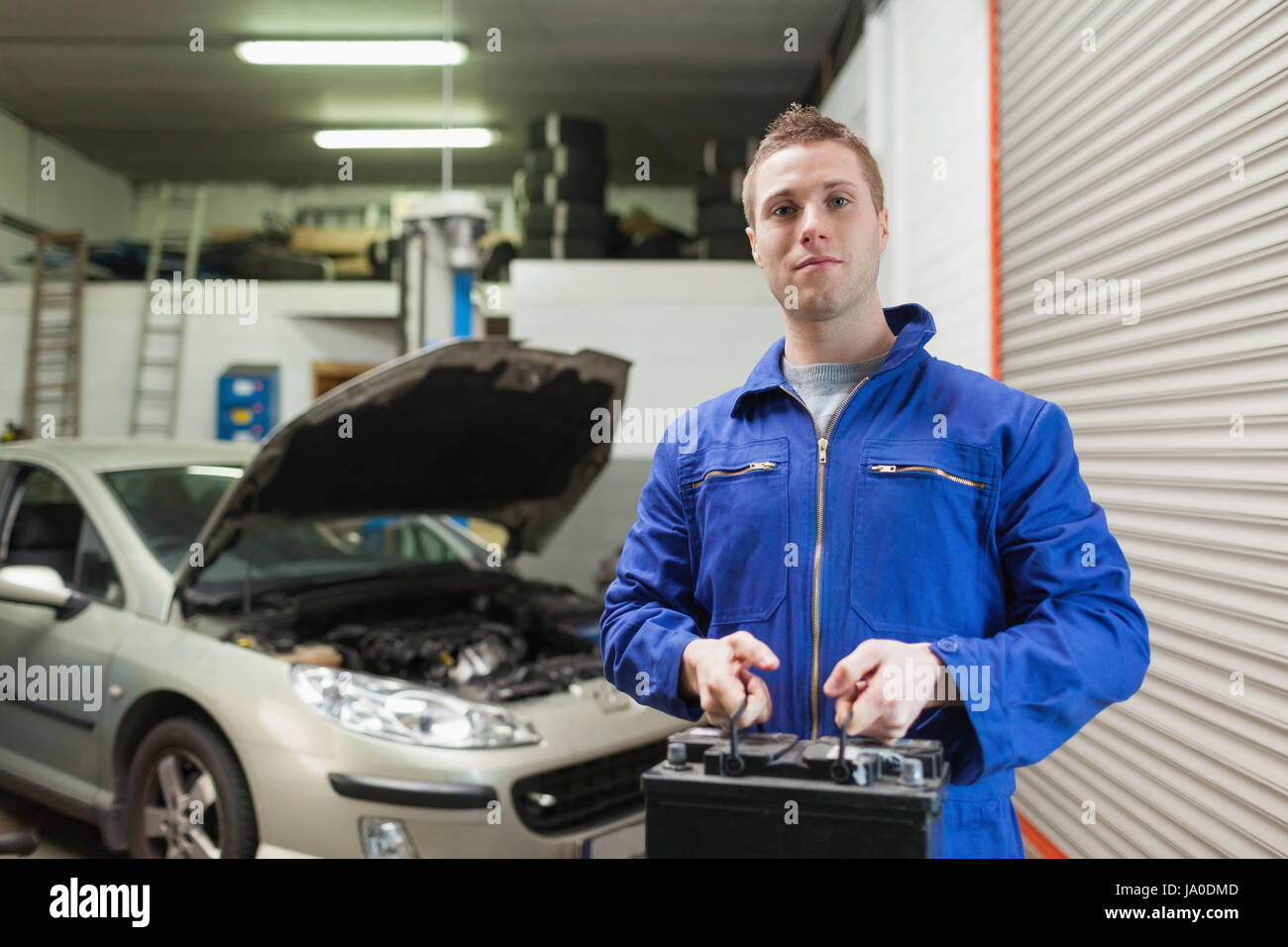 Portrait of male mechanic carrying car battery in workshop Stock Photo ...