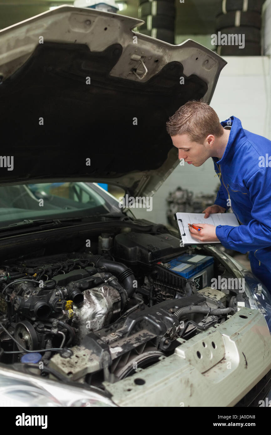 Auto mechanic writing on clipboard while examining car engine Stock ...