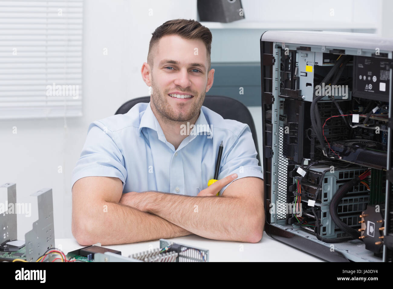 Portrait of smiling hardware professional sitting by an open cpu at ...