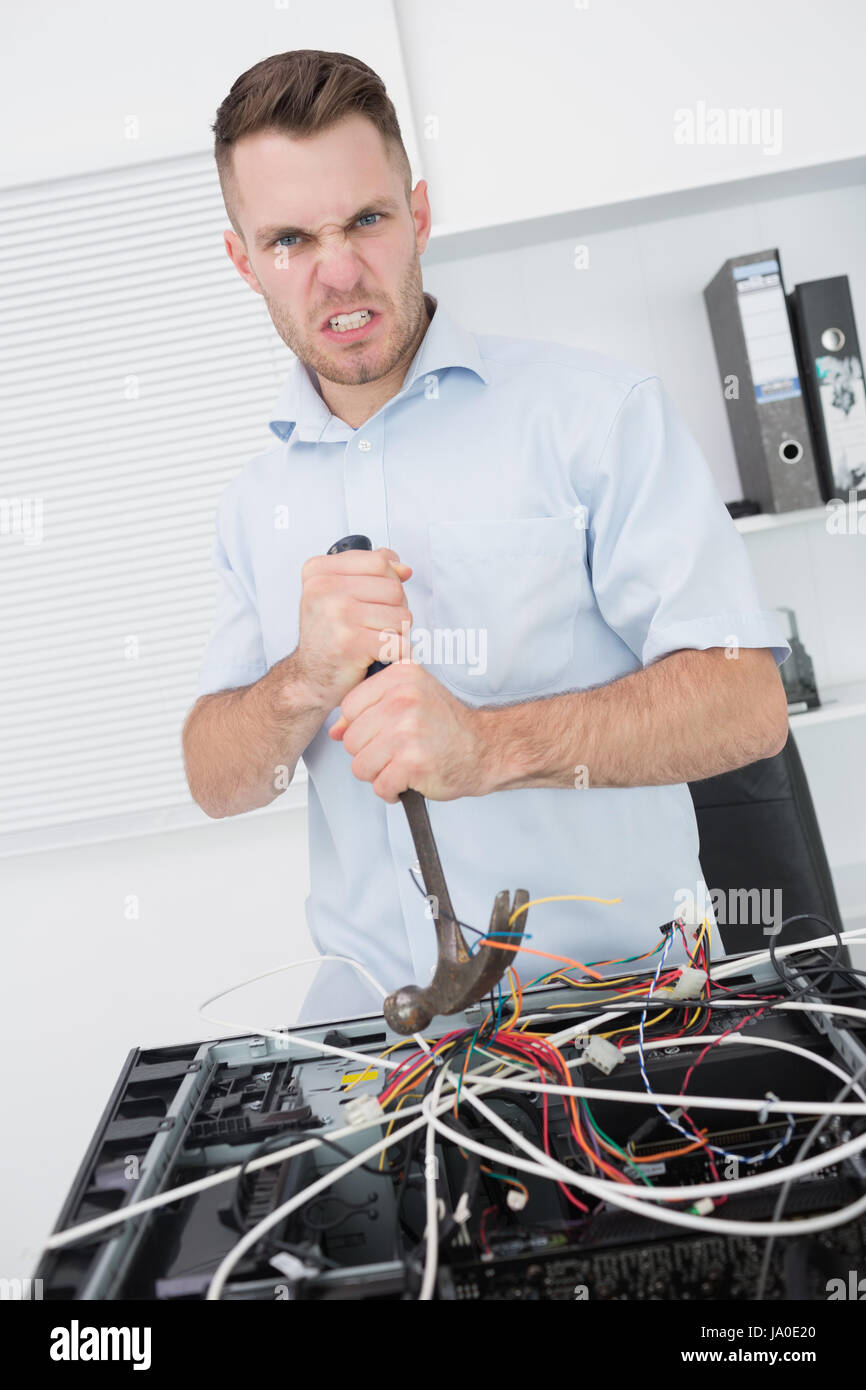 Portrait of frustrated young man using hammer to pull out wires from ...