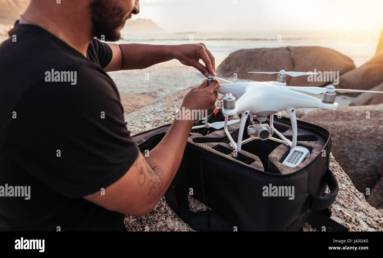 Young man sitting at rocky beach with a drone. Man setting up ...