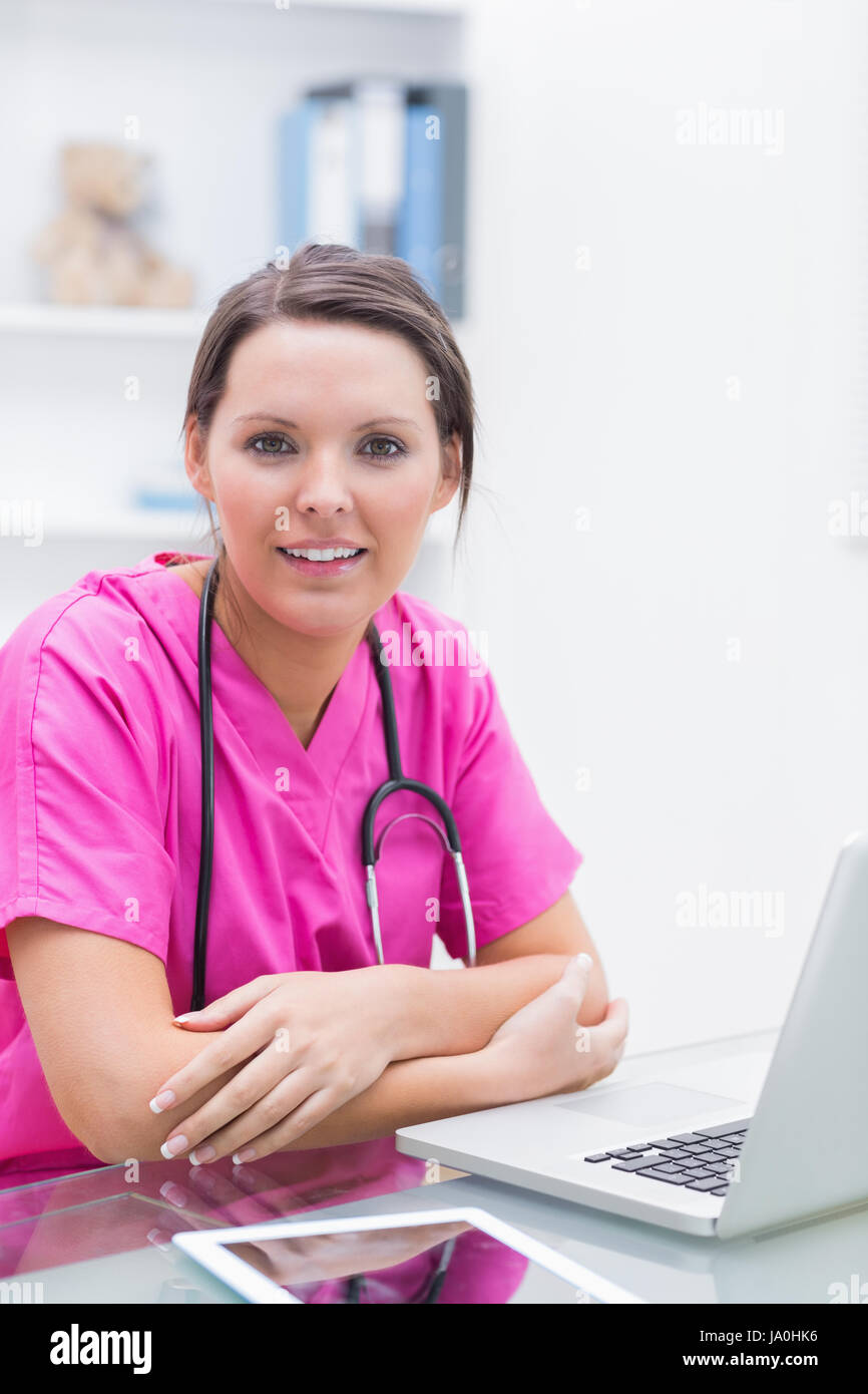 Portrait of smiling young nurse with laptop at desk in clinic Stock ...