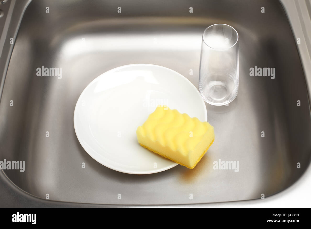 Close up of kitchen sink with clean white plate, yellow cleaning sponge ...