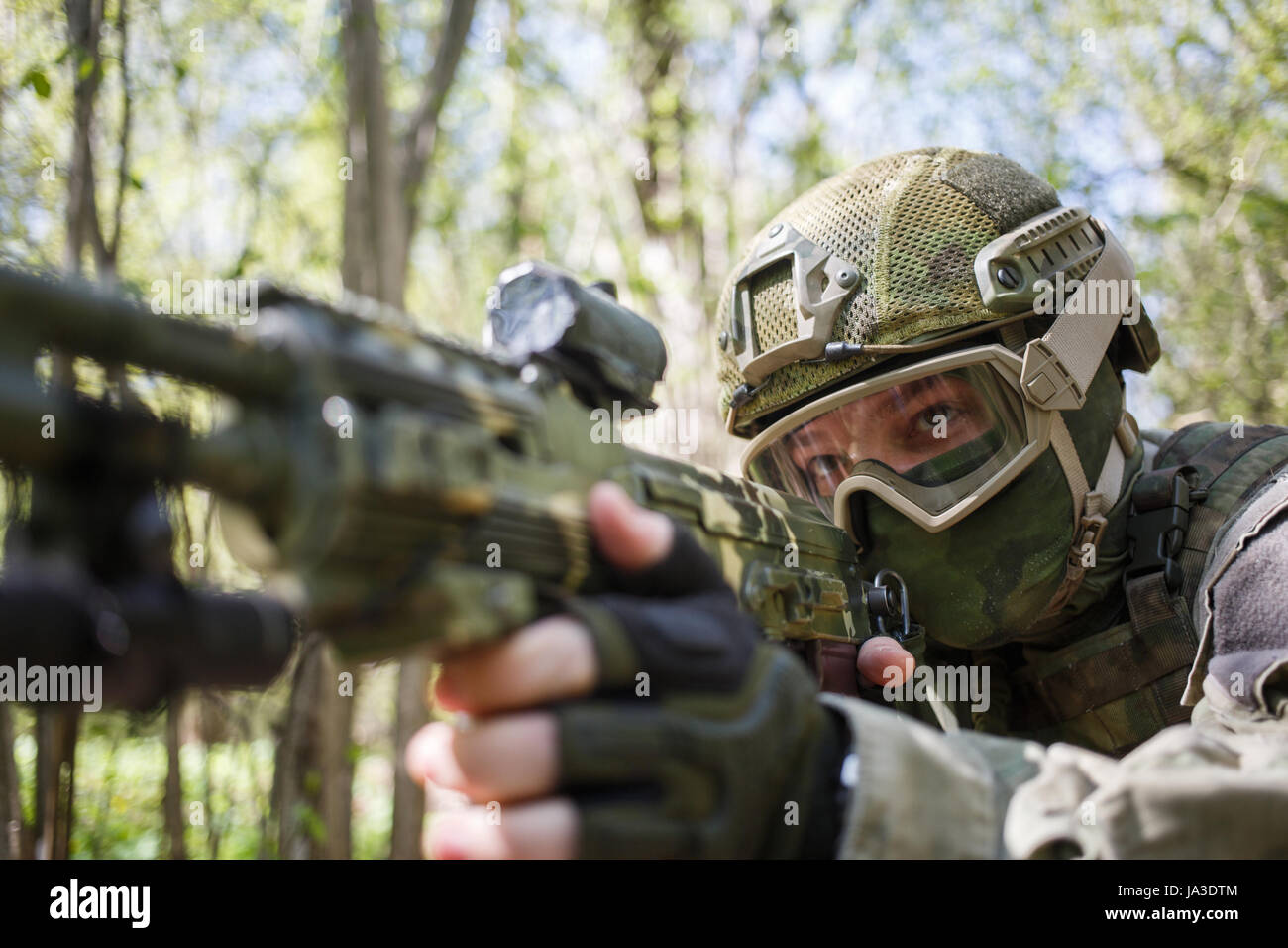 Soldier in helmet takes aim with gun in summer forest during day Stock ...