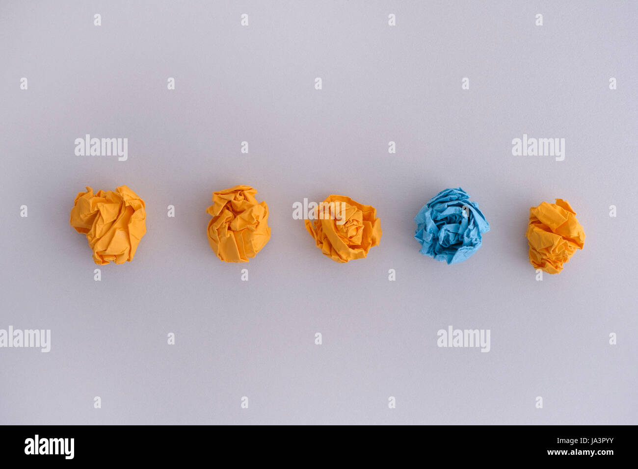 Four crumpled yellow paper balls and one blue on a grey background ...