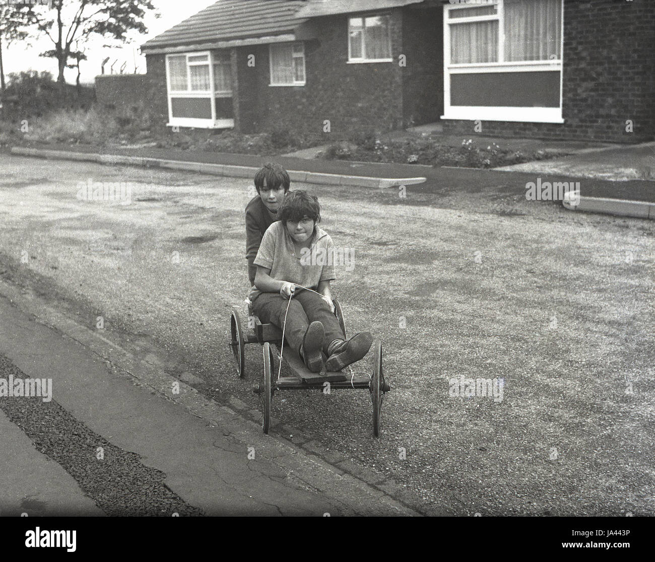 1970s, historical, two young boys riding on a home made wooden go-kart ...