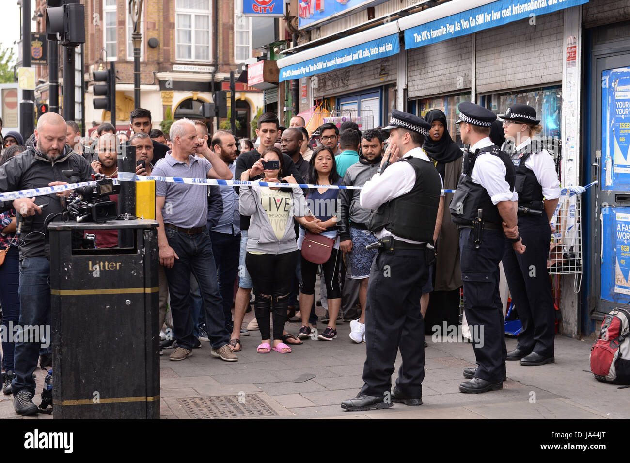 A crowd gathers behind a police cordon on Barking Road in East Ham ...