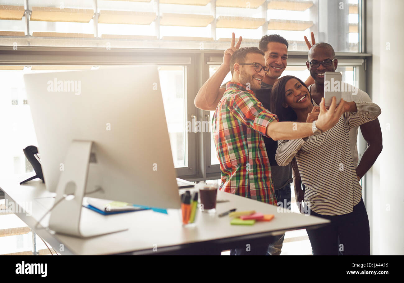 Cheerful office workers gesturing horns and taking selfie at the ...