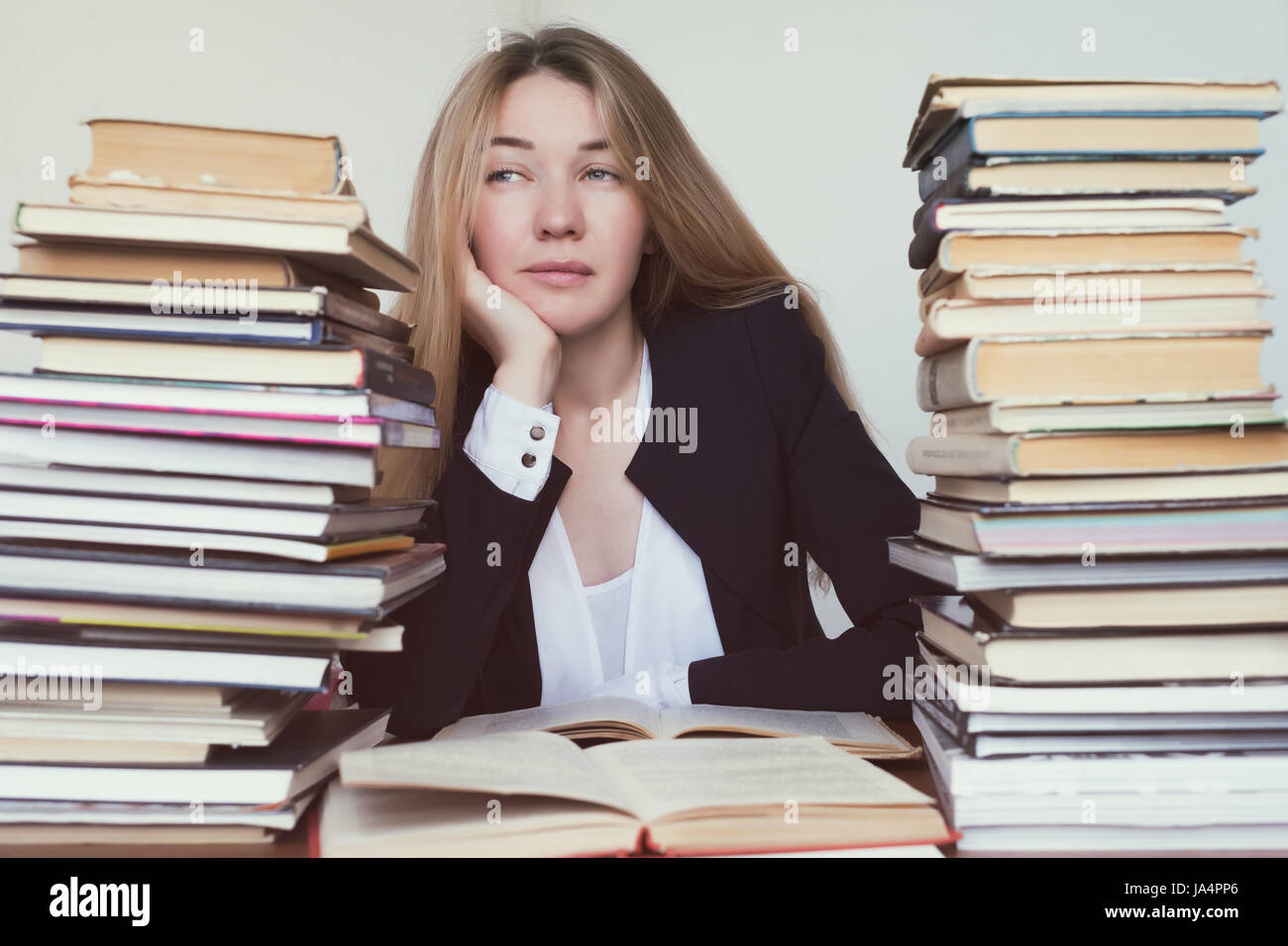 beautiful girl looks up, puzzled, looking out from behind the stacks of ...
