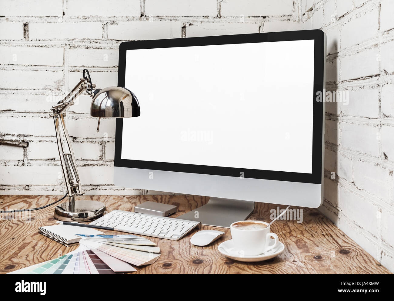 Blank screen computer and lamp on wooden table against brick wall ...