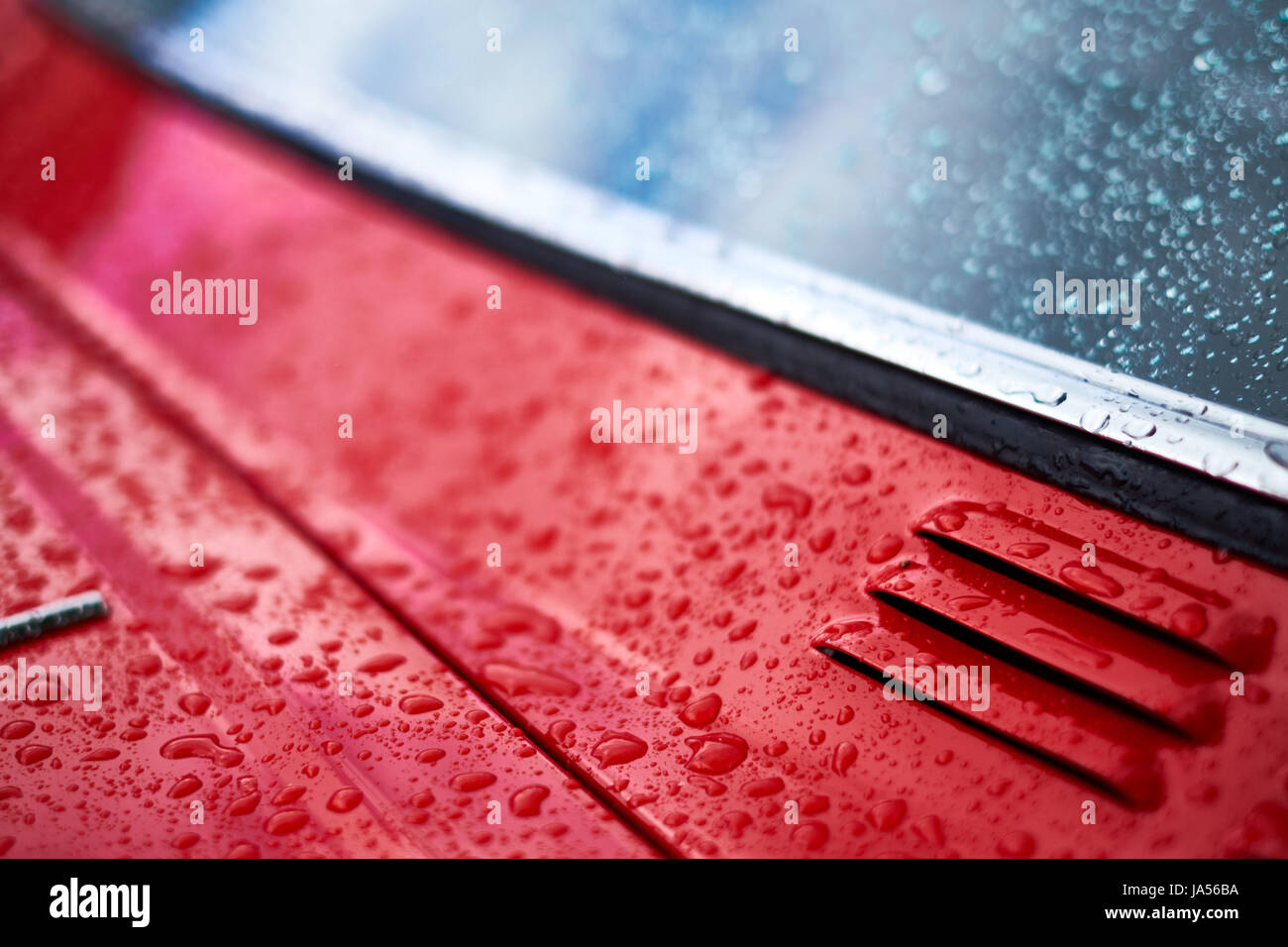 Rain falls on a red car forming water drops, close up of vent and ...