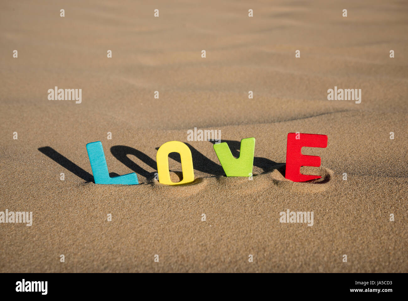 LOVE written out with colourful wooden letters text on sand of a dune ...
