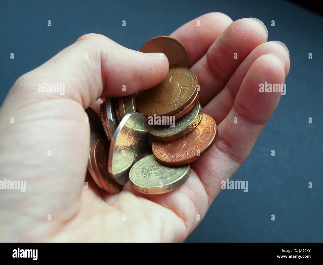 Hand with British Pounds coins (UK currency) over a dark background ...