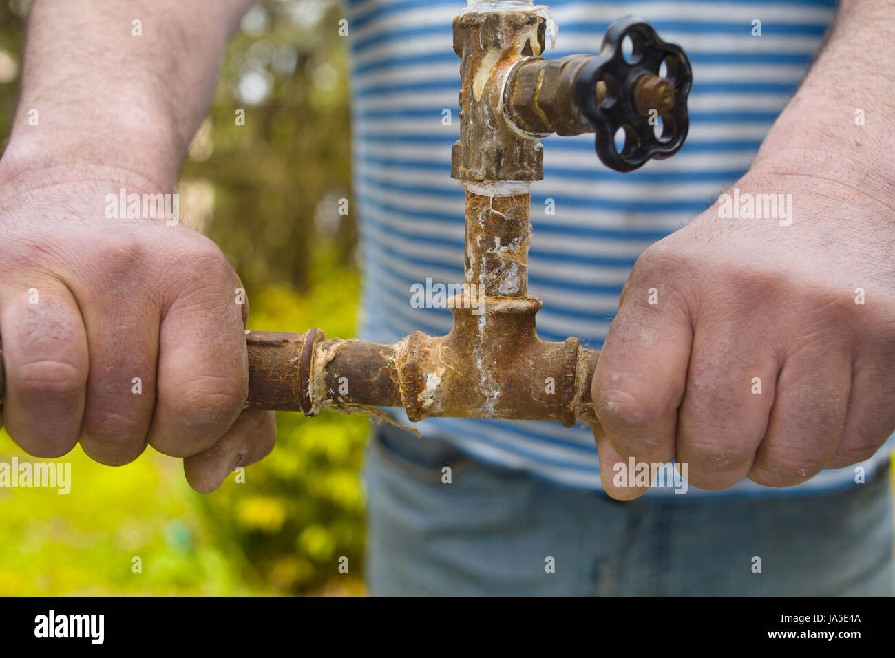 Hands of plumber holding a rusty water pipe, outdoor cropped closeup ...