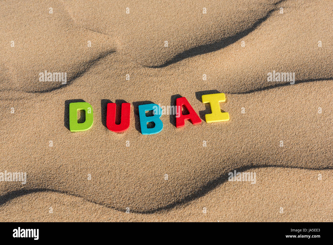 DUBAI word written with colourful letters on soft sand of the desert ...
