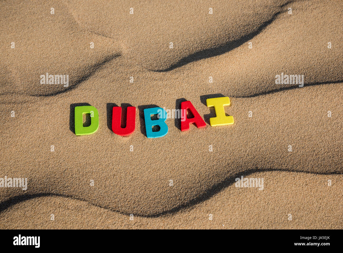 DUBAI word written with colorful letters on soft sand of the desert ...