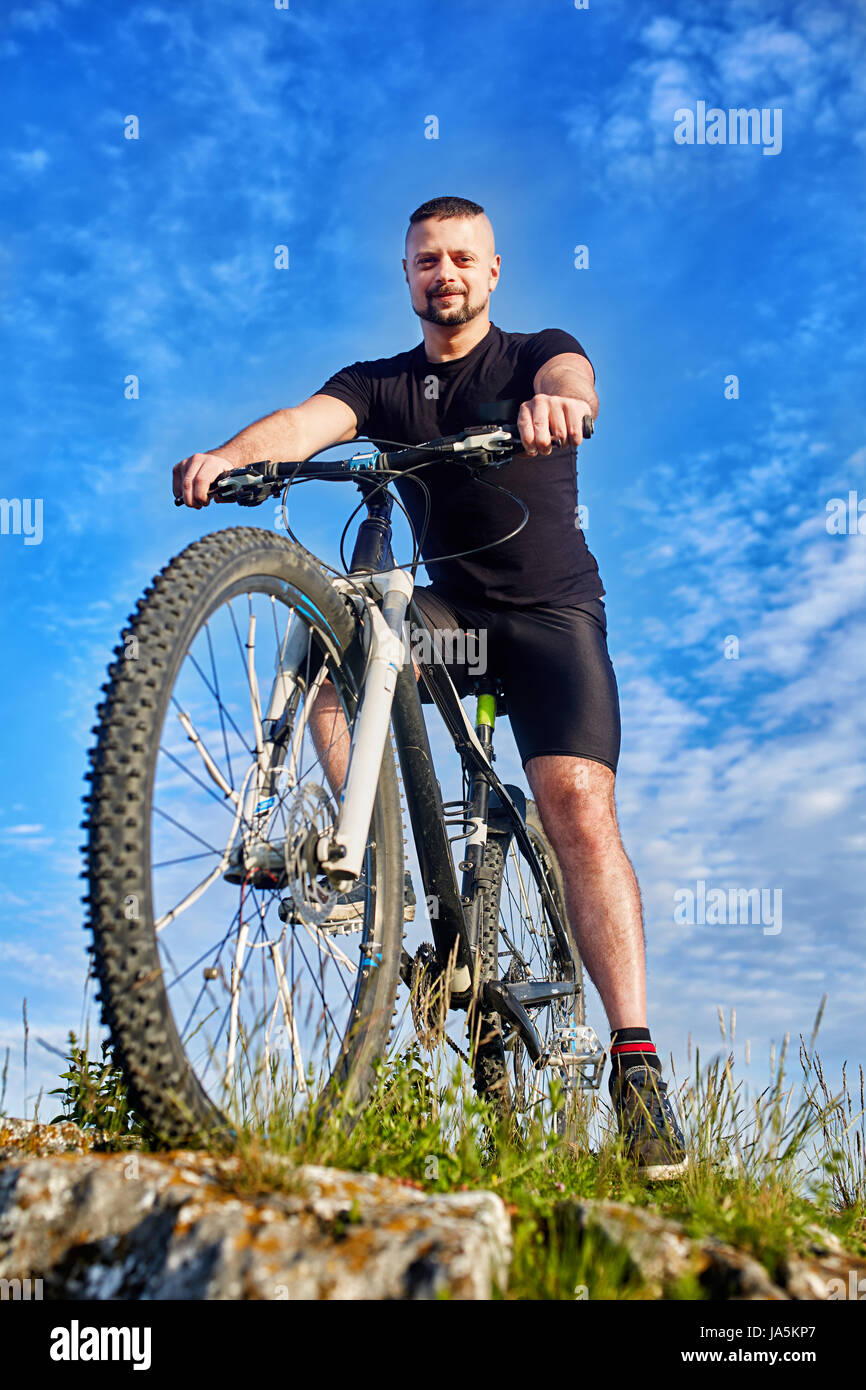 Bottom view of the smiling cyclist with bike against blue sky with ...