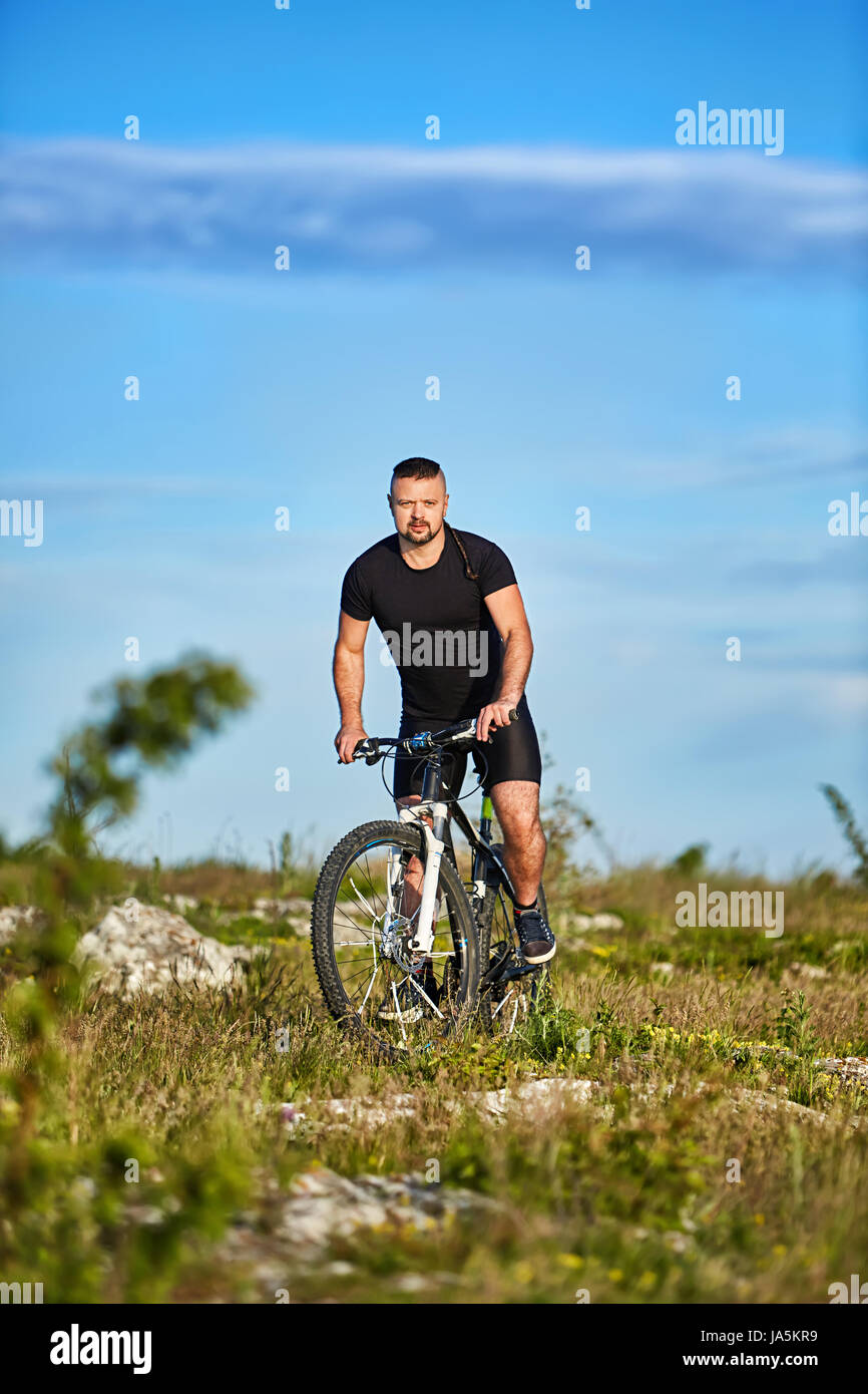 Attractive sportsman riding bike on rocky trail against sky with clouds ...