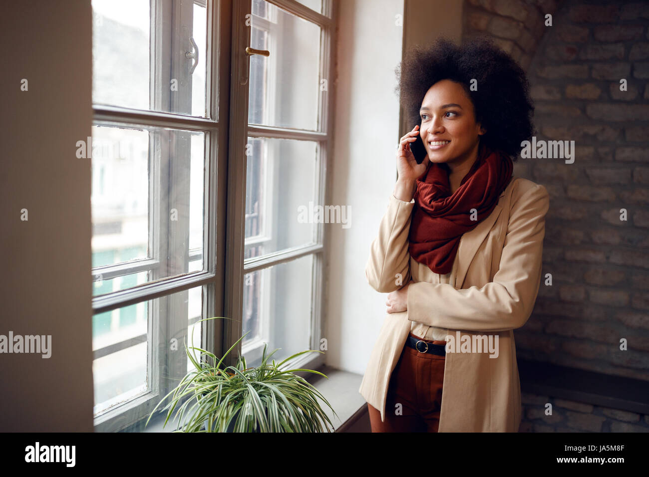 African girl looking through window while talking on cell phone Stock ...