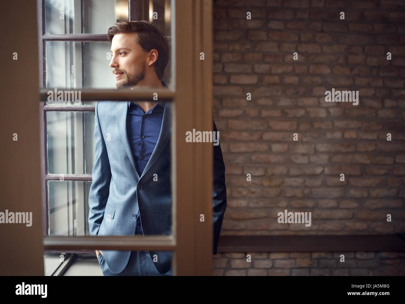 Man in business suit looking through window in office Stock Photo - Alamy