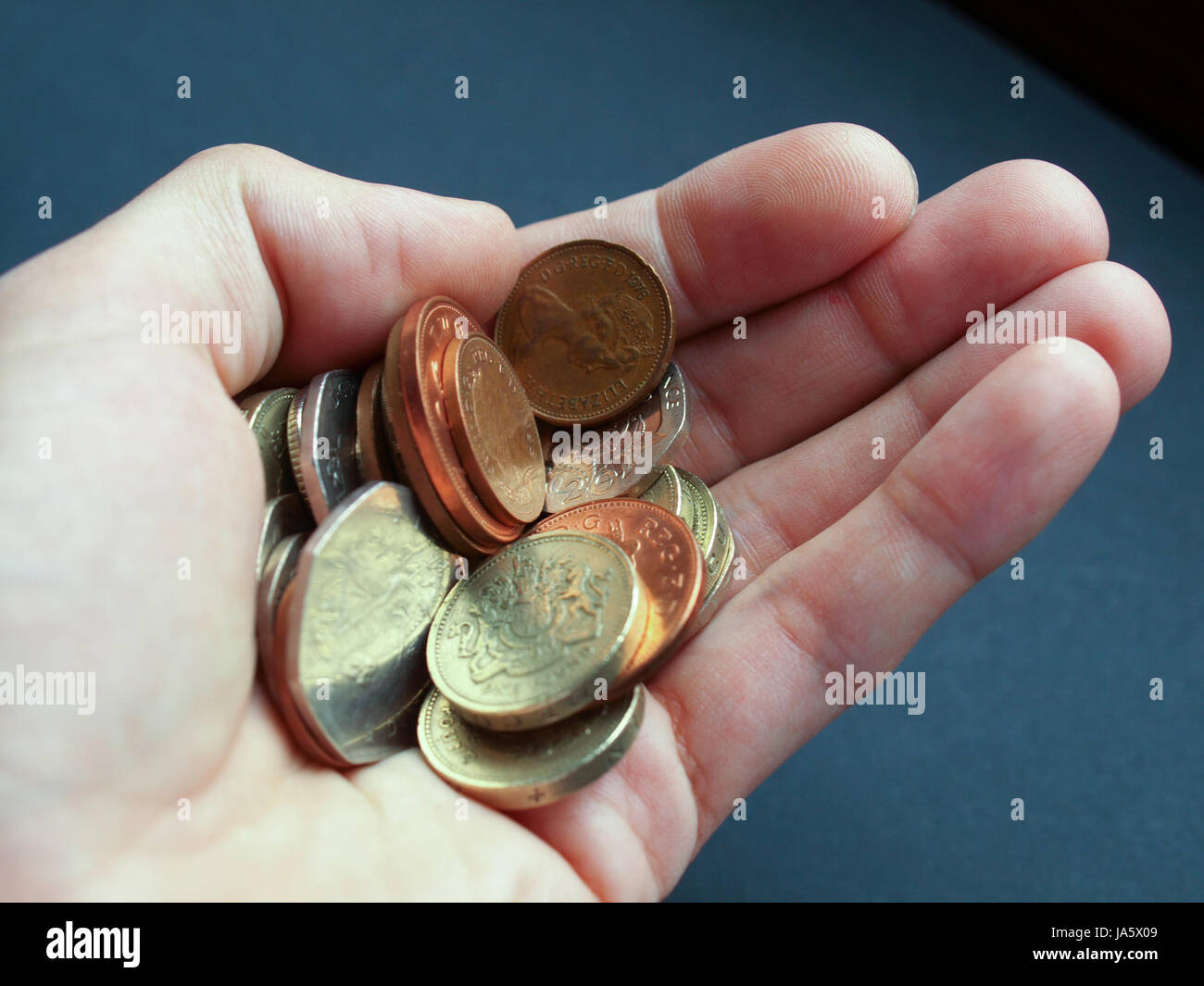 Hand with British Pounds coins (UK currency) over a dark background ...