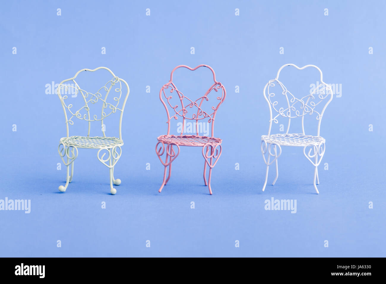 Pink and white decorative mini wrought iron chairs on purple background ...