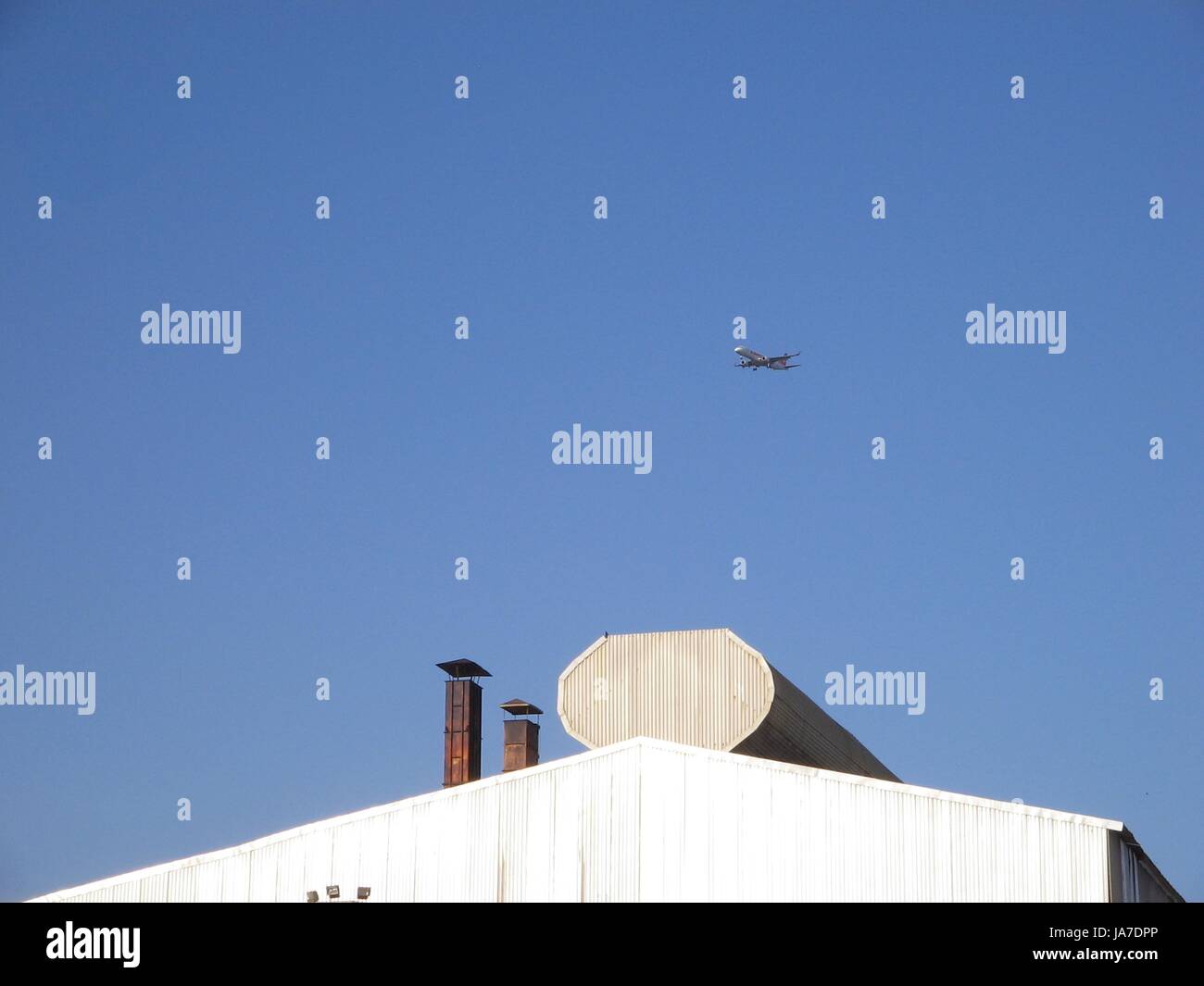 Airplane flying over industrial warehouse Stock Photo - Alamy