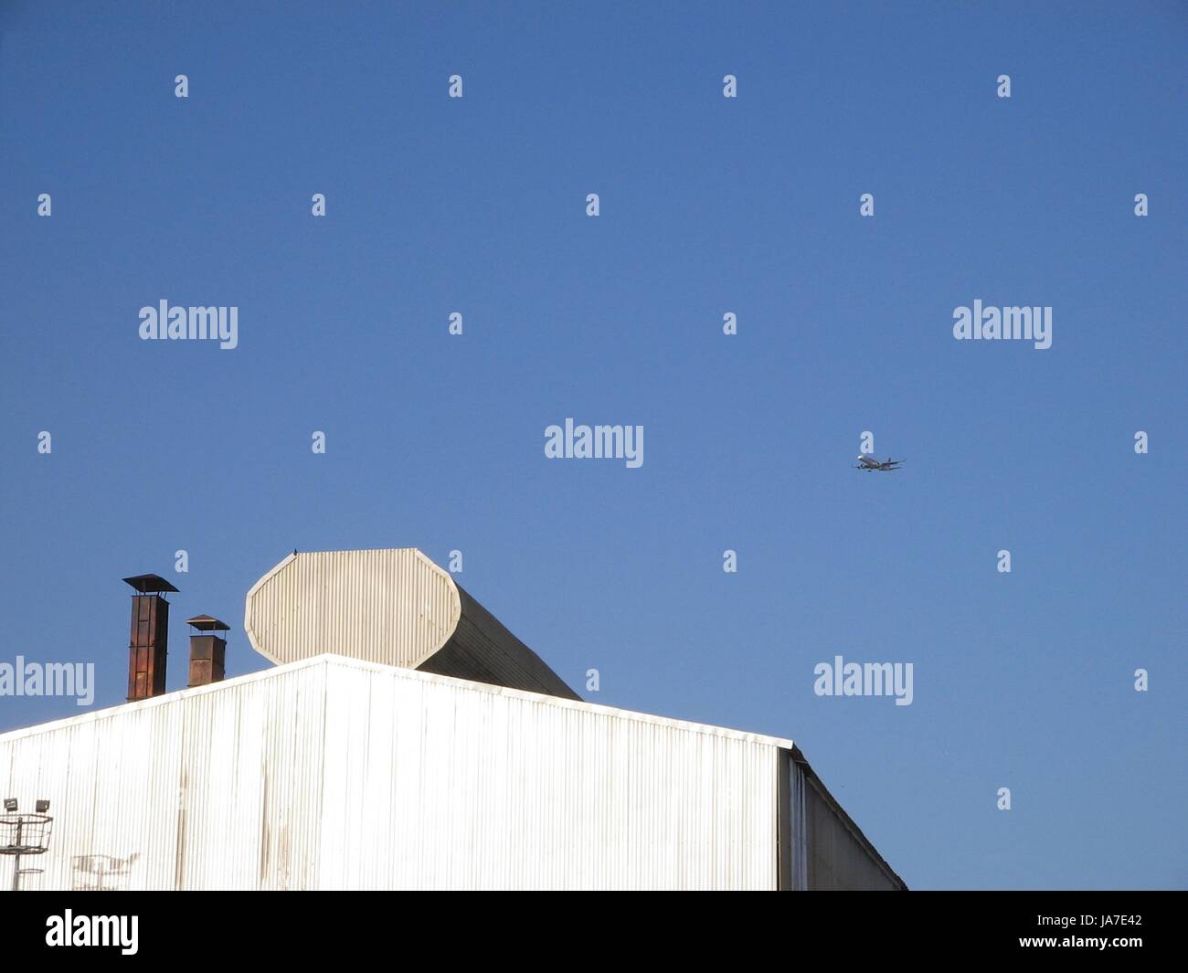 Airplane flying over industrial warehouse Stock Photo - Alamy