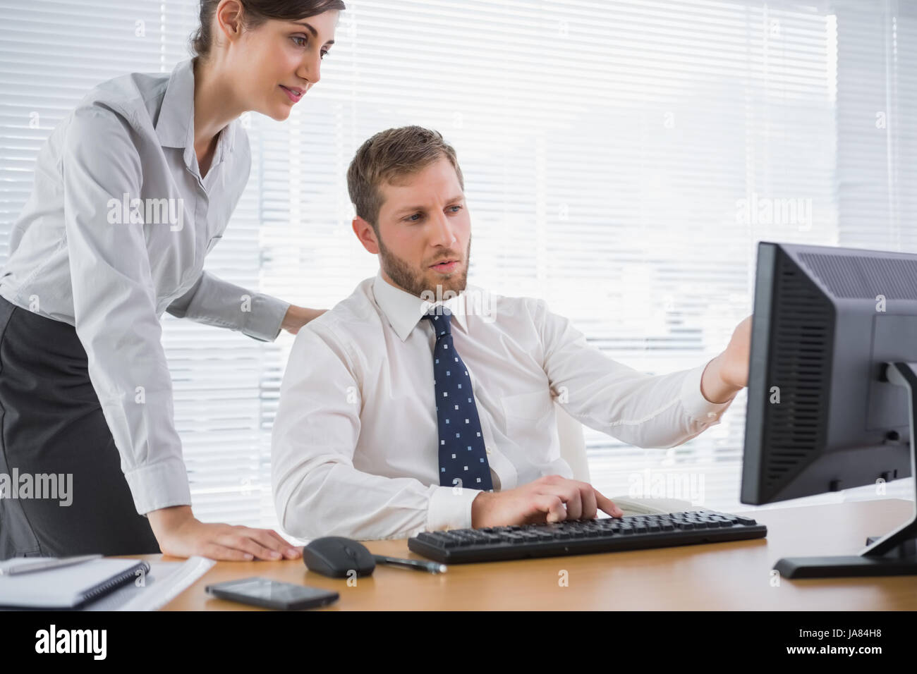 Businessman showing his colleague something on computer at desk in ...