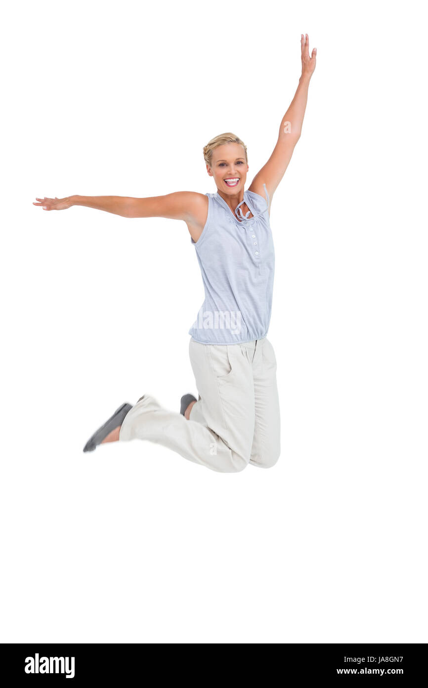 Happy blonde woman jumping with hands up in air on white background ...