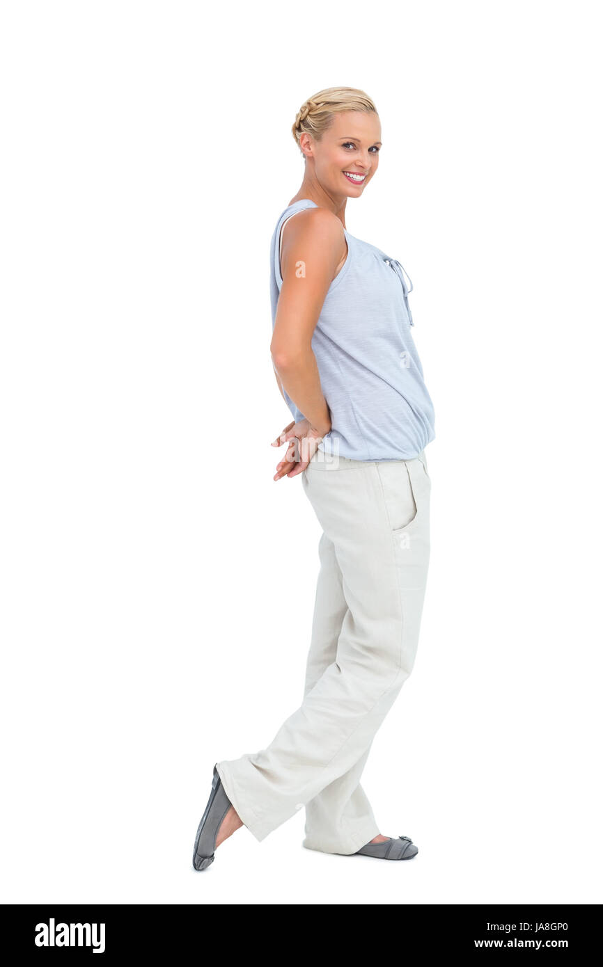 Woman looking at camera with hands behind her back on white background ...