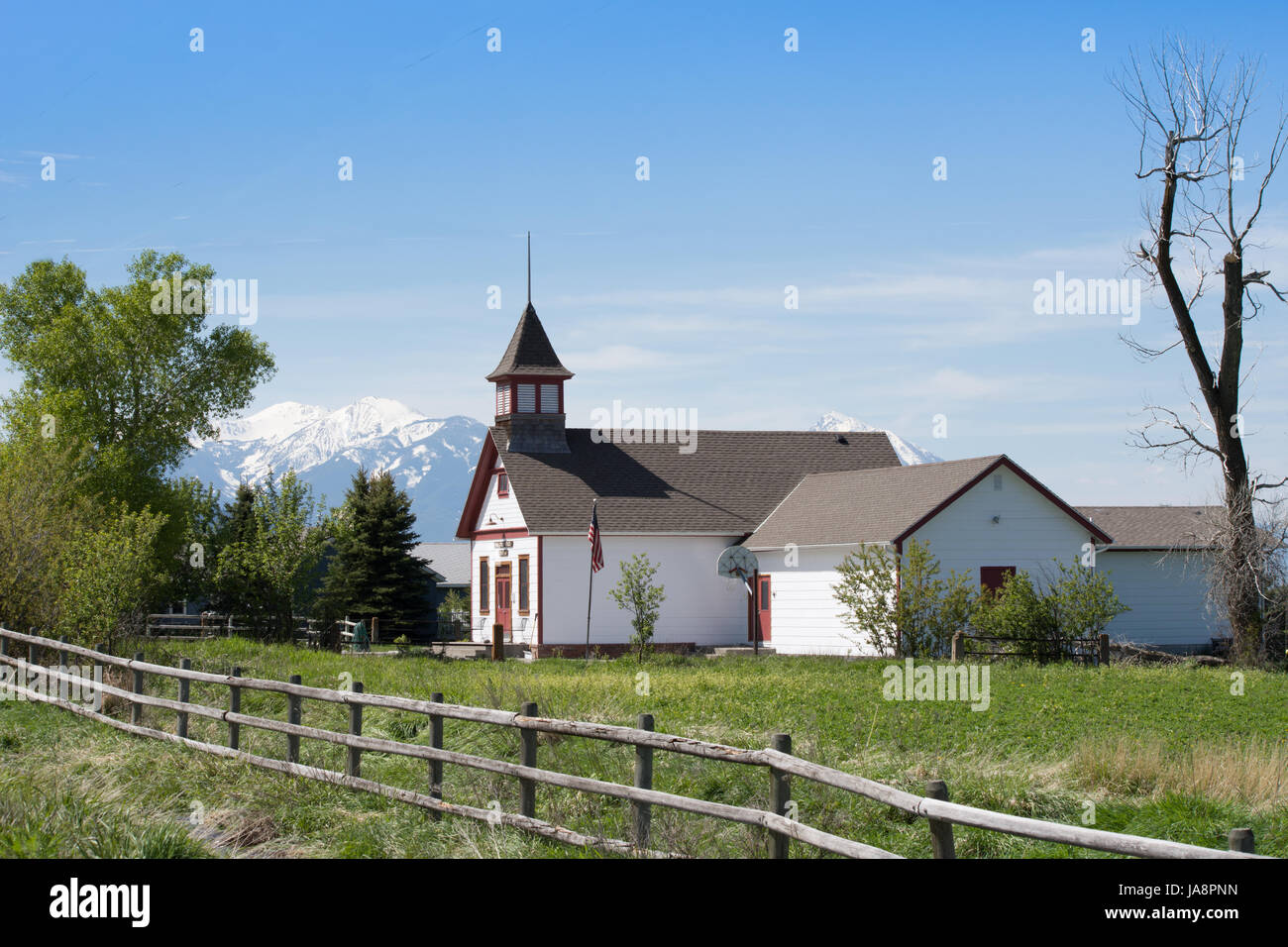 A country school house painted white with red trim, a flag and ...