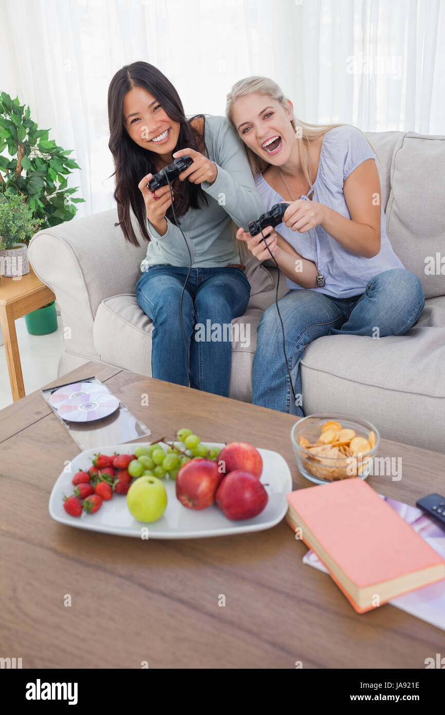 Happy friends playing video games and laughing at home on the couch ...