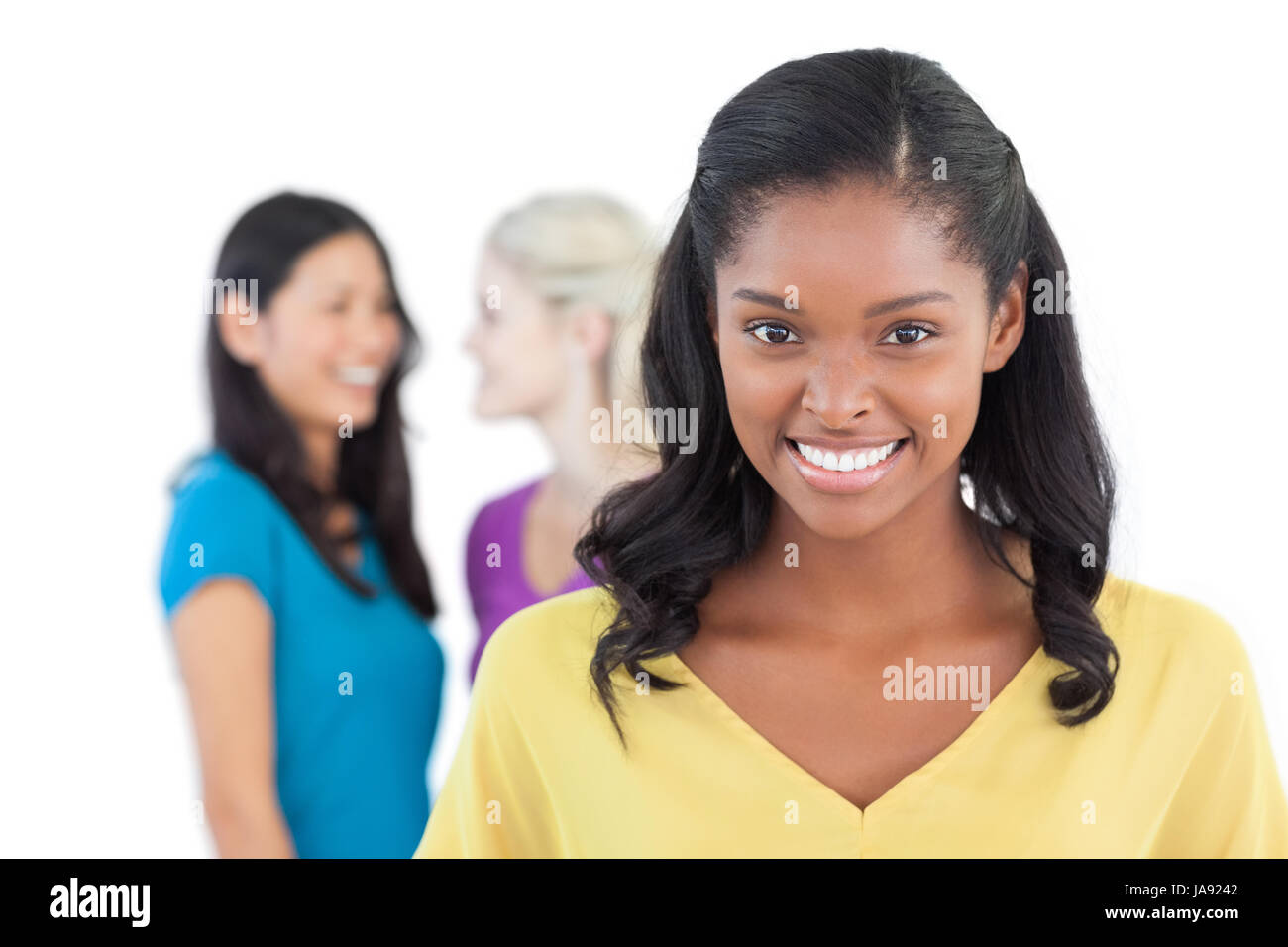 Smiling dark woman looking at camera with two women behind her on white ...