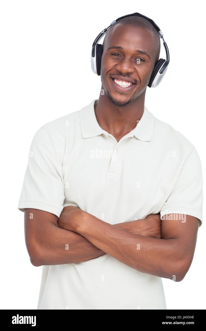 Smiling man listening to music with arms crossed on a white background ...