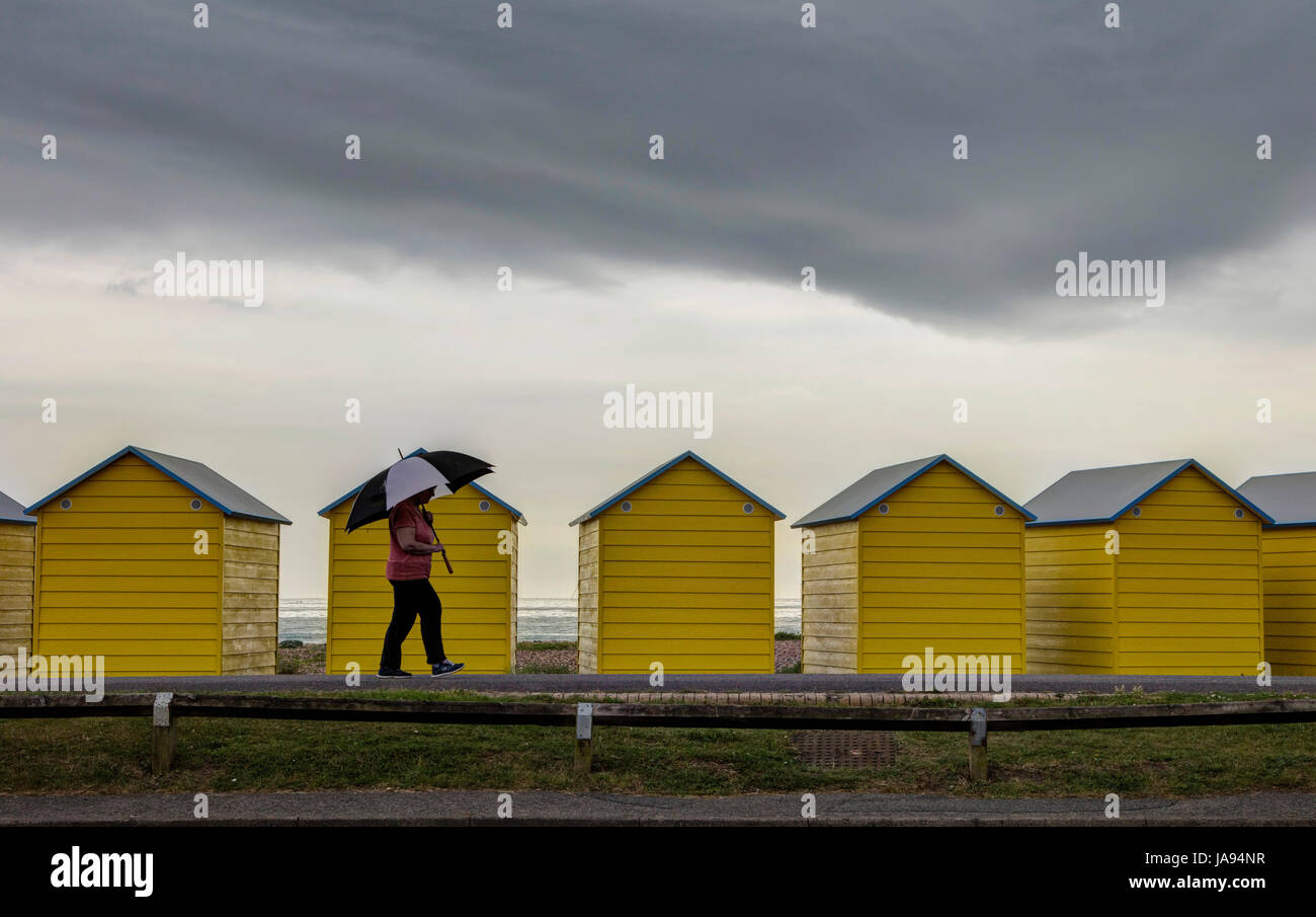 Lady walking with umbrella up in rain by beach huts Stock Photo - Alamy