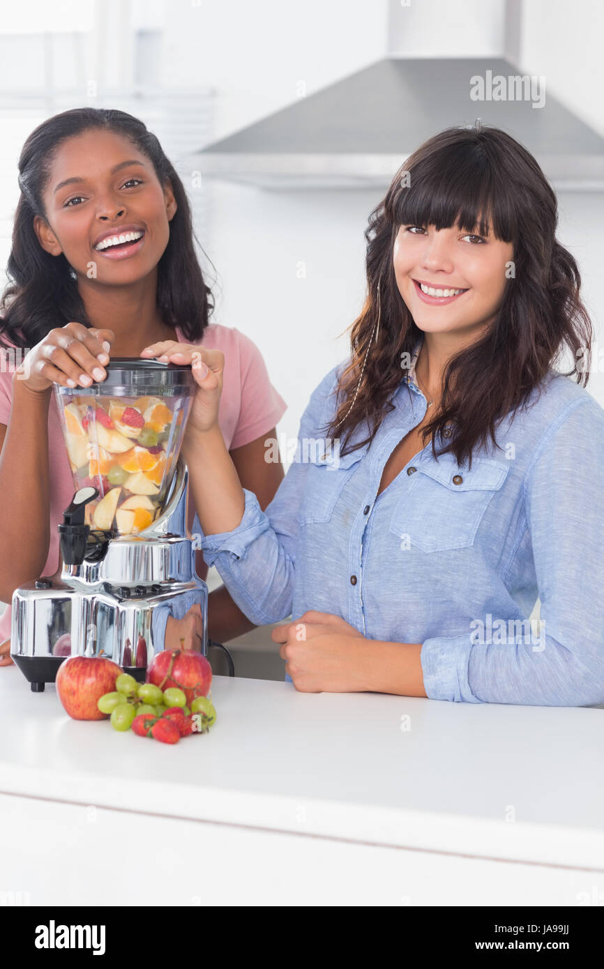 Cheerful friends about to make healthy juice looking at camera in ...
