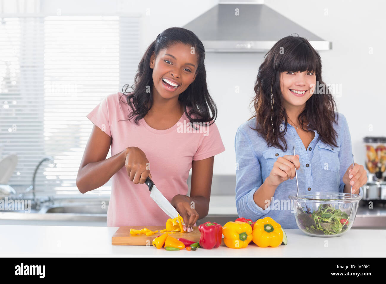 Happy friends preparing a salad together at home in kitchen smiling at ...