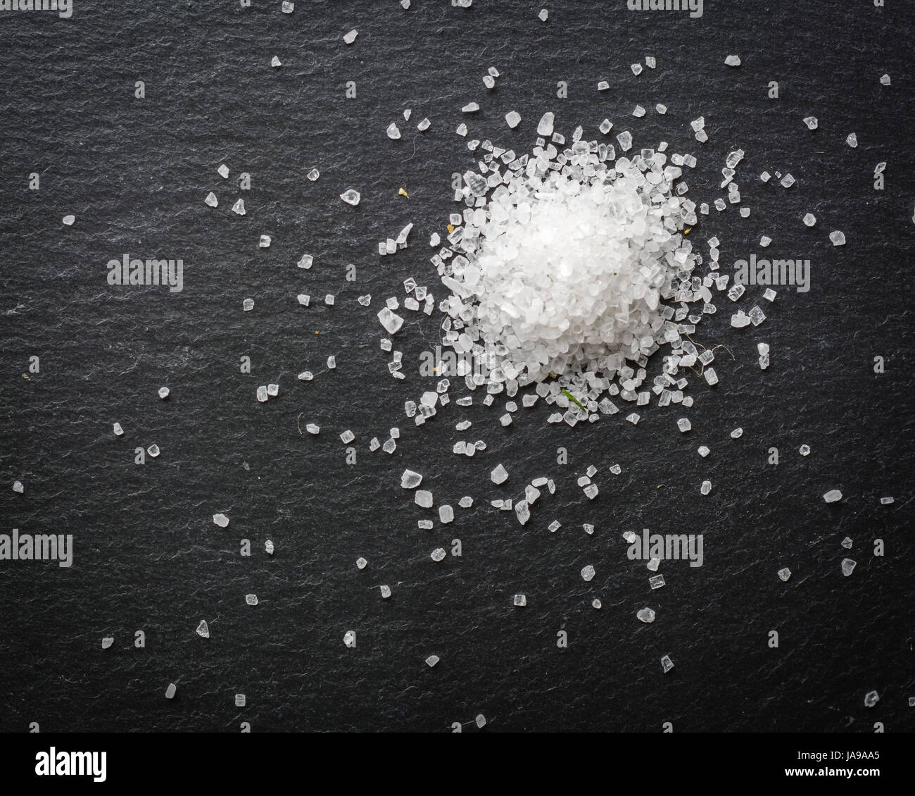 A bunch of white salt crystals on a black stone background. Seasoning ...