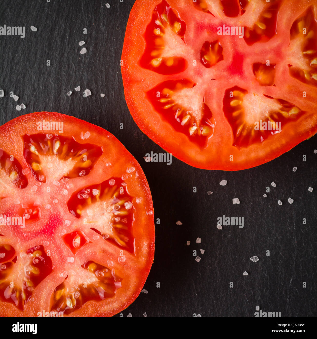 Cut tomato red with seeds and patterns. View from above. Black stone ...